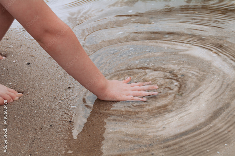 The child dips his hand into the water and tries the sand. The concept ...
