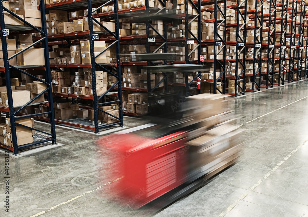 Blur of a motorized stock picker between aisles of cardboard boxes on ...