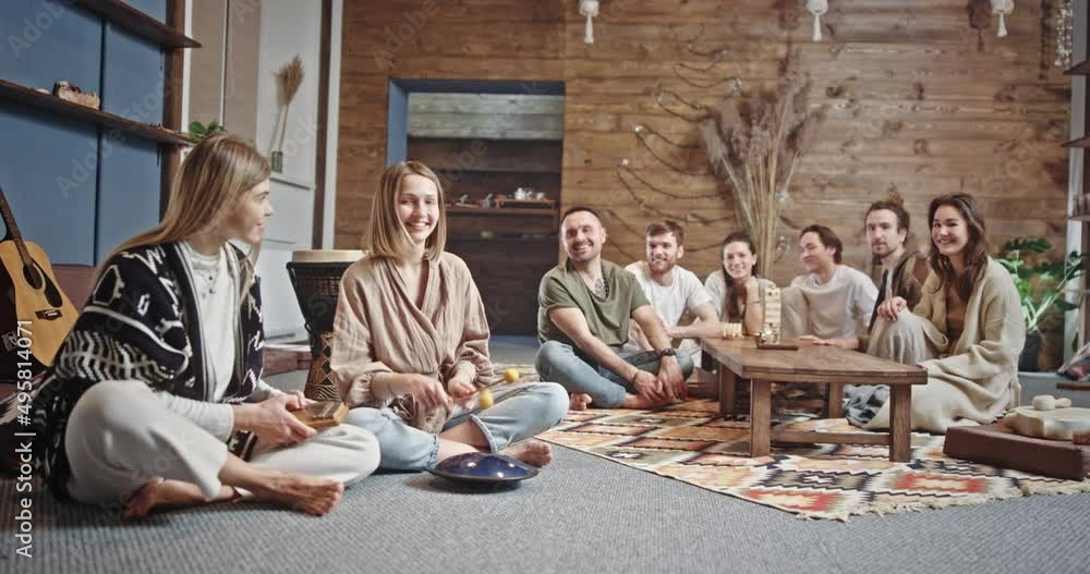 Group of happy modern young friends sitting on the floor and playing ...