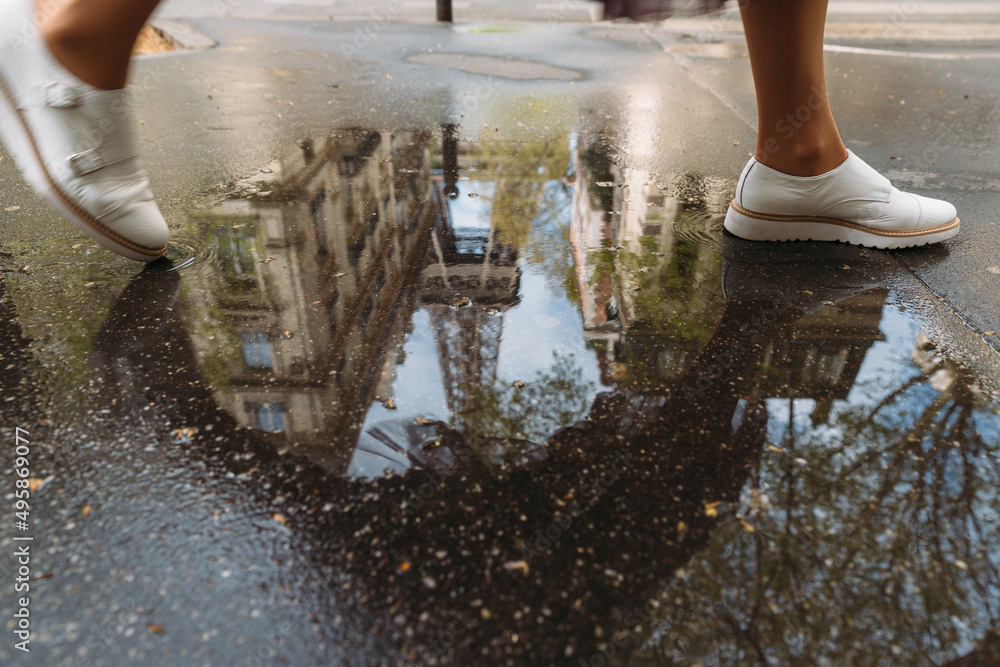 Close up photo of girl stepping over a puddle. In the puddle reflected ...