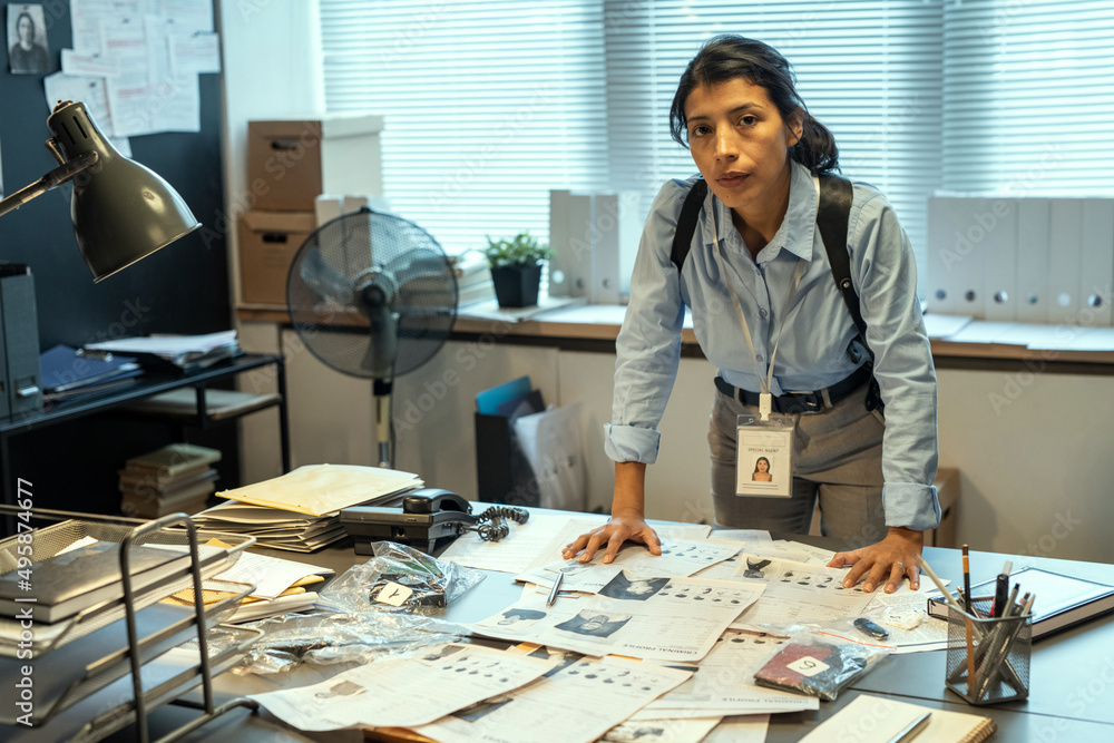 Young serious female agent of FBI in uniform bending over workplace ...