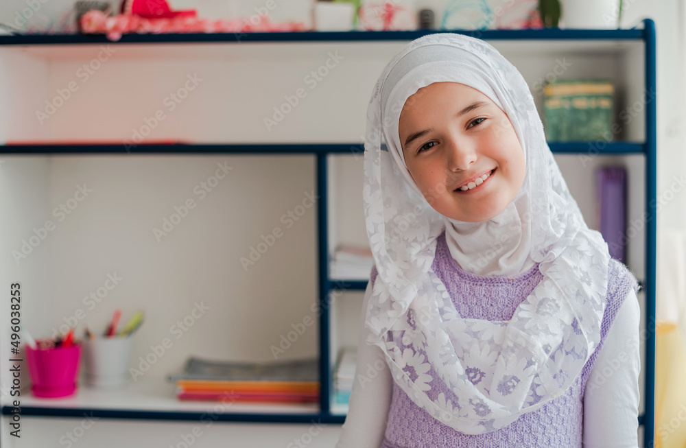 Portrait of a smiling Muslim student girl wearing modern hijab at home ...