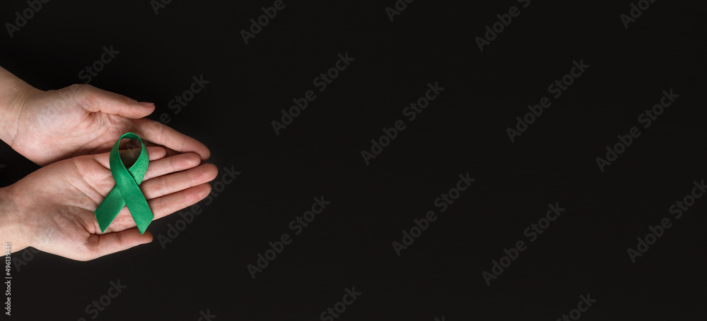 World bipolar day. Adult hands holding green ribbon on black background ...