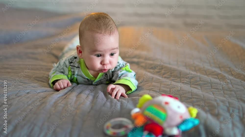 Tiny boy lies on the bed and toy is in front of him. Cute kid moving ...