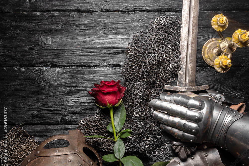 Knight sword, red rose flower and iron helm on the black woorden flat ...