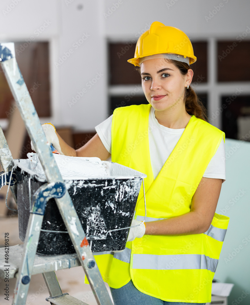 Smiling young female builder in yellow vest and hard hat near step ...