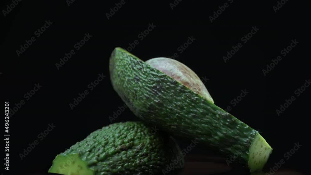 Two halves of an avocado rotate in a circle on a black background. A ...