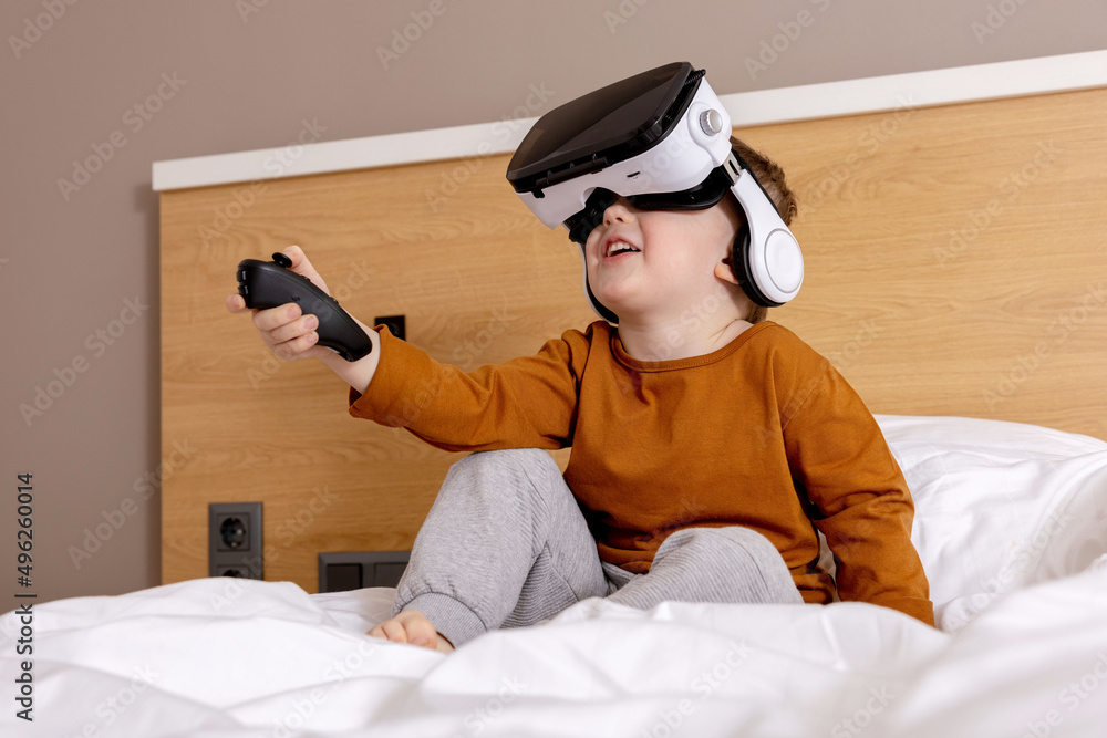 Little adorable boy sitting on bed at home with VR headset and playing ...