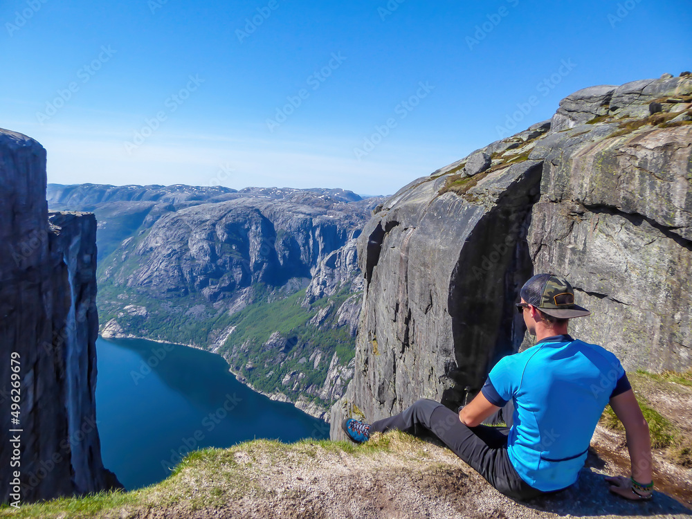 A young man sitting at the edge of a steep mountain. His legs are ...