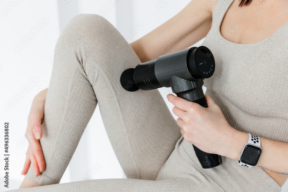 A girl in a tracksuit massaging with a vibrating massager. An electric therapeutic pistol ...