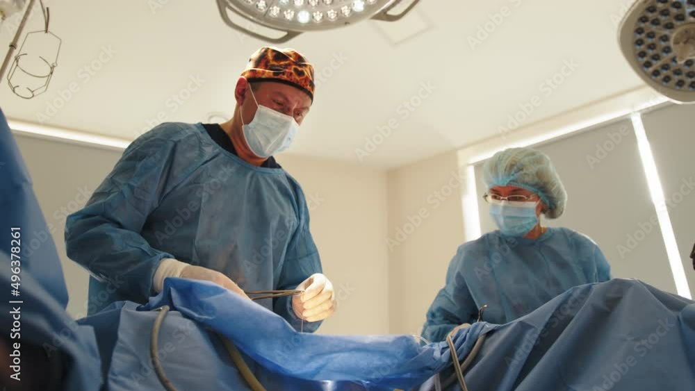 Low angle of the concentrated surgeon man with his assistants sutures ...