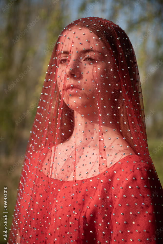 woman in red dress hidden under veil outside in nature with green ...