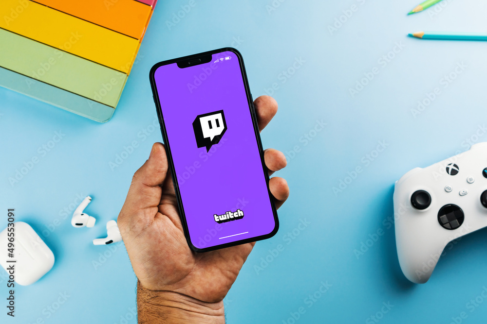 Man holding a smartphone with Twitch app on the screen. Blue background ...