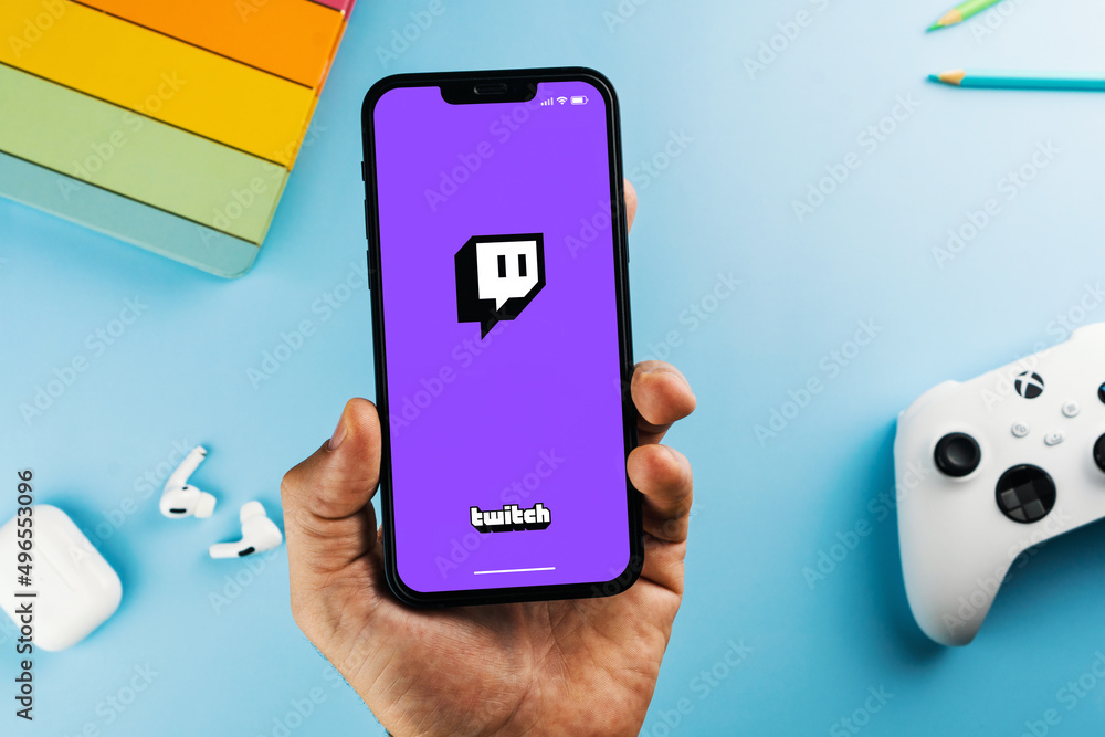 Man holding a smartphone with Twitch app on the screen. Blue background ...