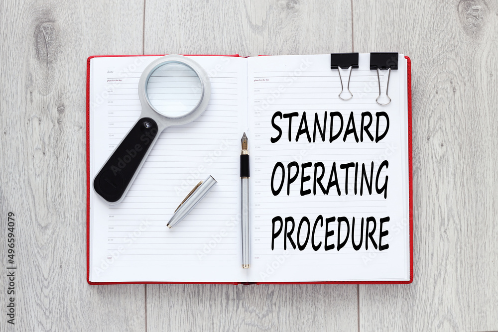 SOP - Standard Operating Procedure, text on an open red notebook on a ...