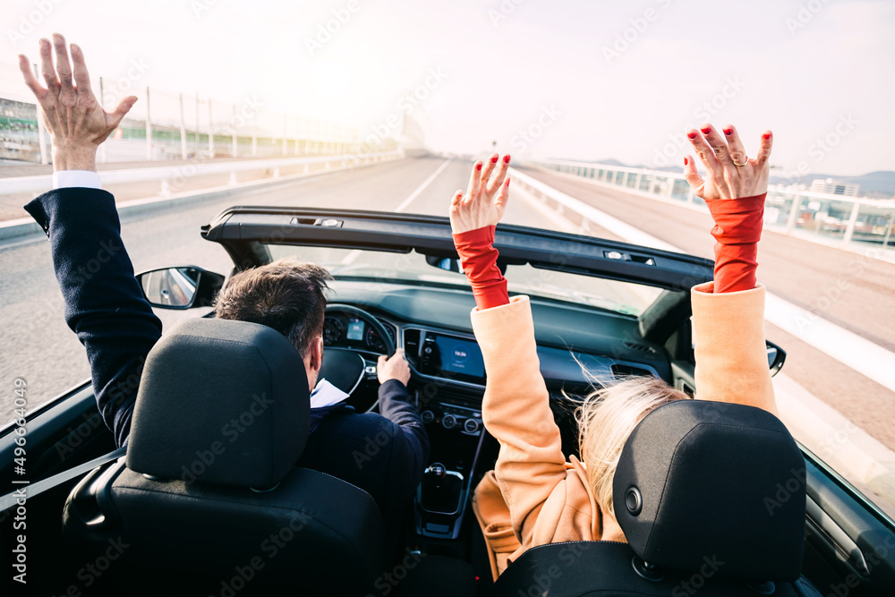 Back view of middle age couple raising their hands up while driving a ...