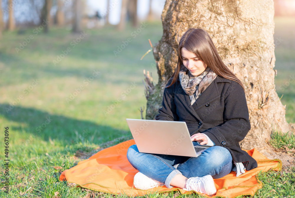 Beautiful young brunette woman working on laptop sitting at the foot of ...
