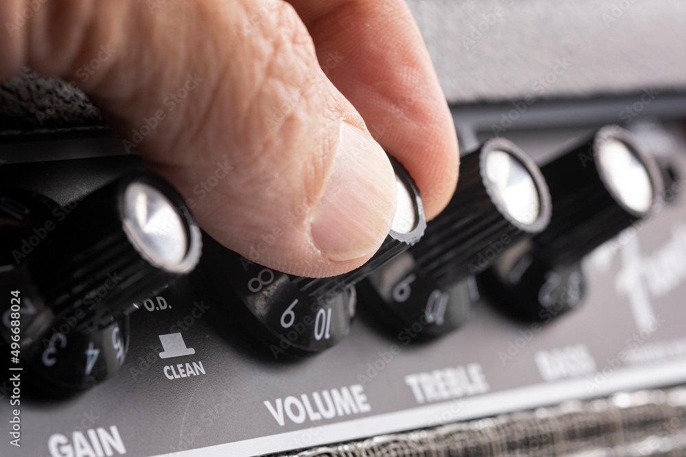 hand turning up the volume of a guitar amplifier, treble and bass ...