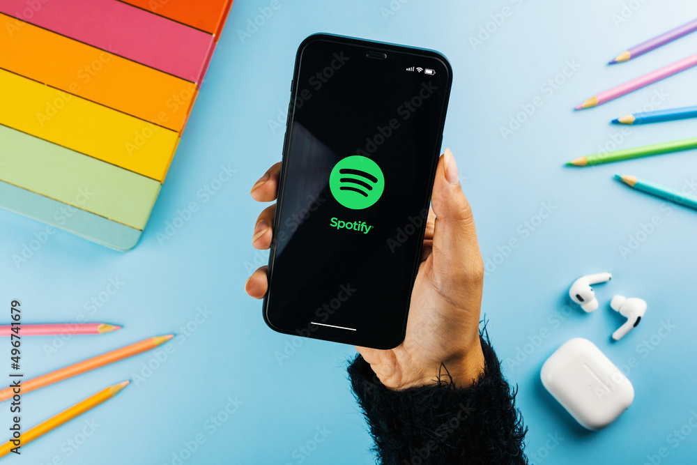 Girl holding a smartphone with Spotify Music app on the screen. Blue ...
