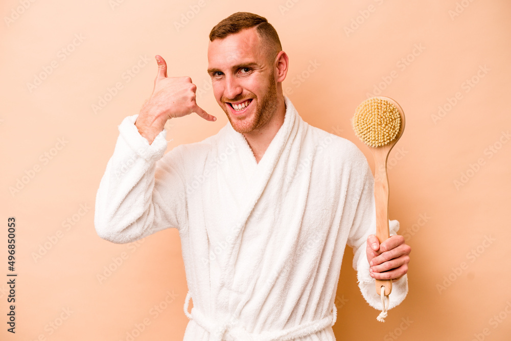 Young caucasian man holding back scratcher isolated on beige background ...