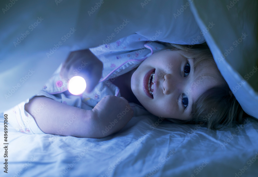Young girl under cover with light in bed at night Stock Photo | Adobe Stock