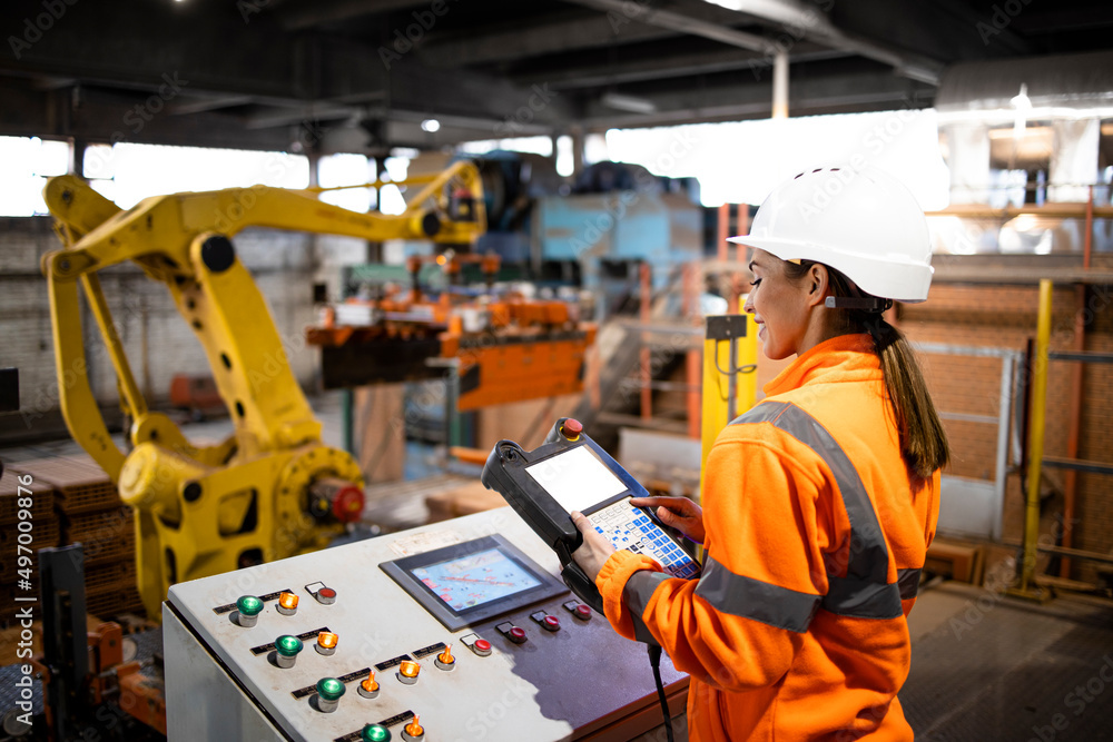 Female factory worker operating industrial robot machine and observing ...