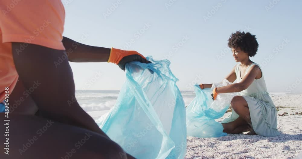 African american couple segregating waste with gloves on sunny beach ...