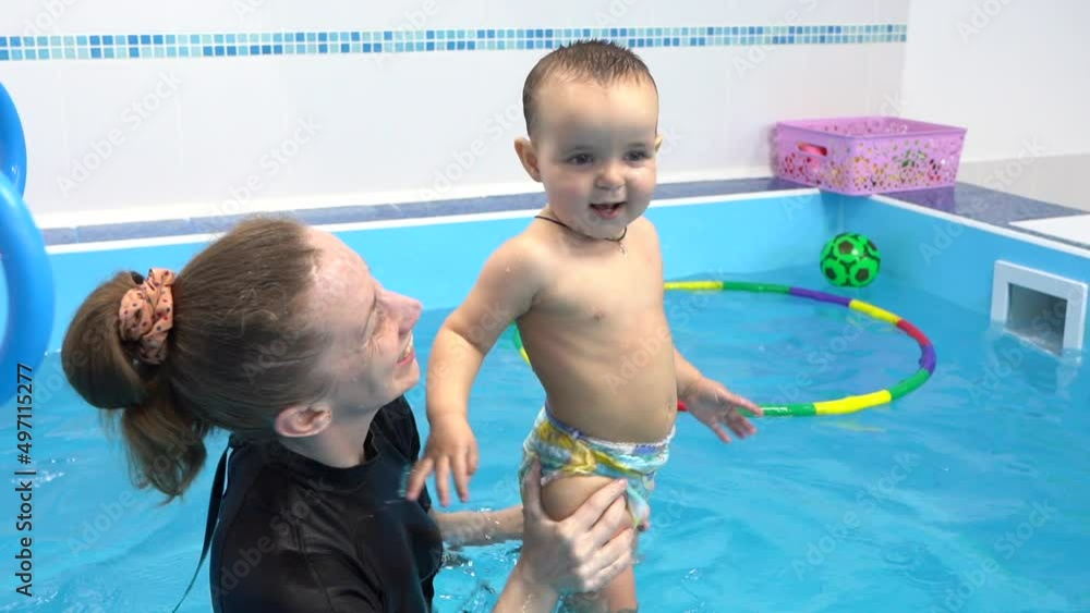 European happy mother in black swimsuit holds a baby boy by the legs in ...