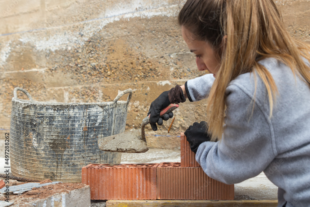 Woman learning for the first time to make a brick wall to make her diy ...