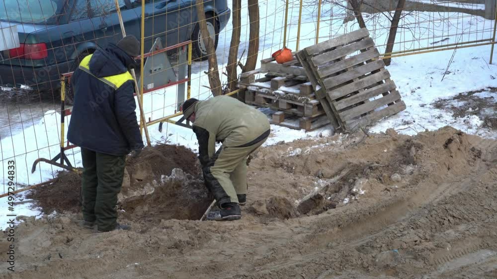 Two builders dig a hole with shovels in the frozen solid ground in ...