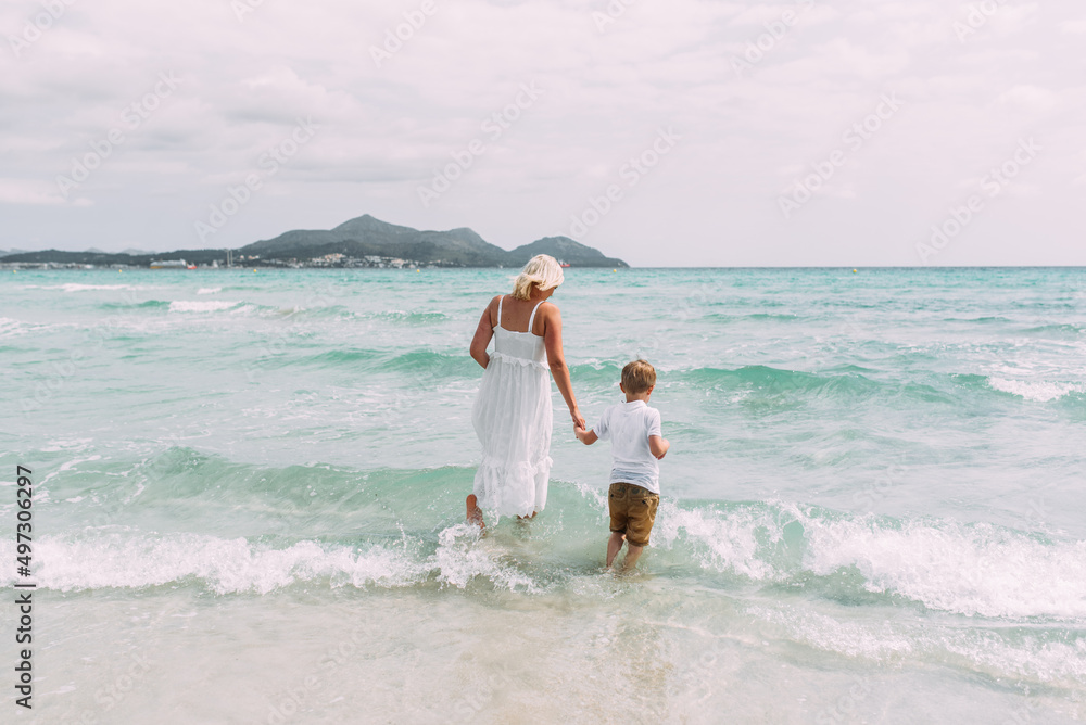 Mama und Kind mit weißen Kleid am Strand im wasser und Wellen spielend ...
