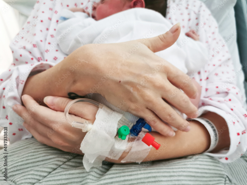 Woman holding her newborn baby with peripheral venous catheter on her ...