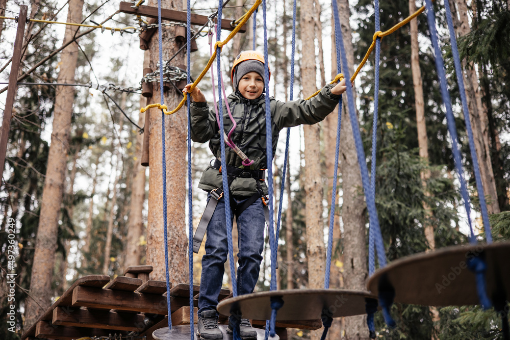 Teenager boy in safety equipment routing and climbing in adventure rope ...