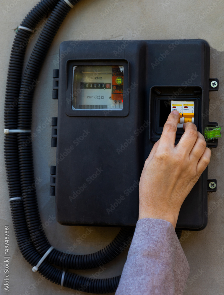Electric meter. A woman's hand turns on a toggle switch on an electric ...