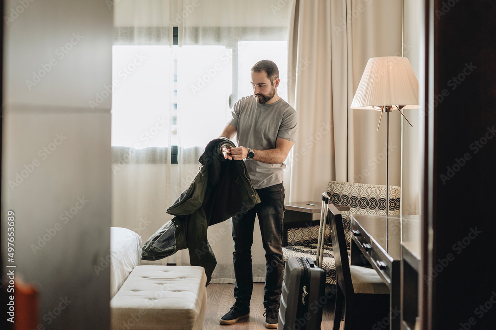 Man taking off jacket in hotel room during work trip Stock Photo ...