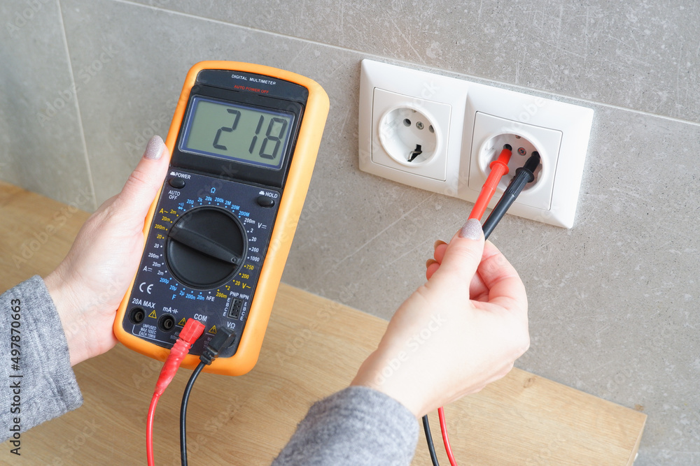 Woman with a multimeter check the voltage of the electrical network ...