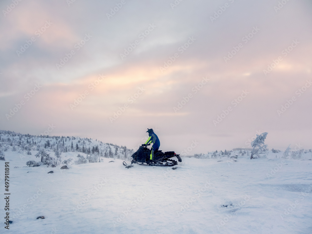 Male on snowmobile in the evening polar hill. Alone man riding up a ...