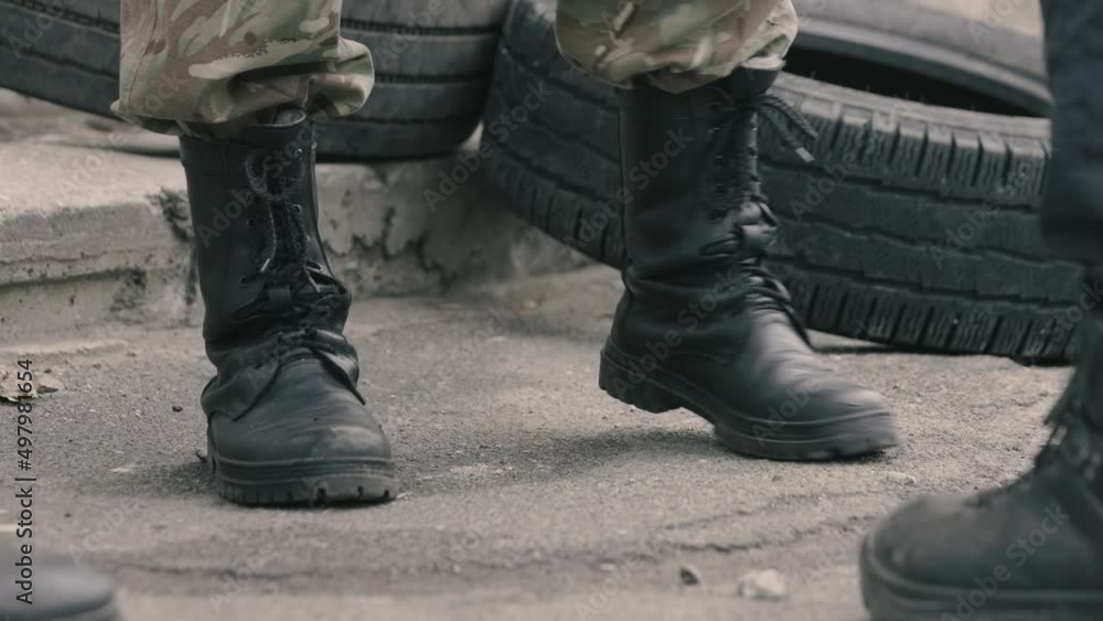 close-up. military feet shod in heavy army boots. old car tires ...
