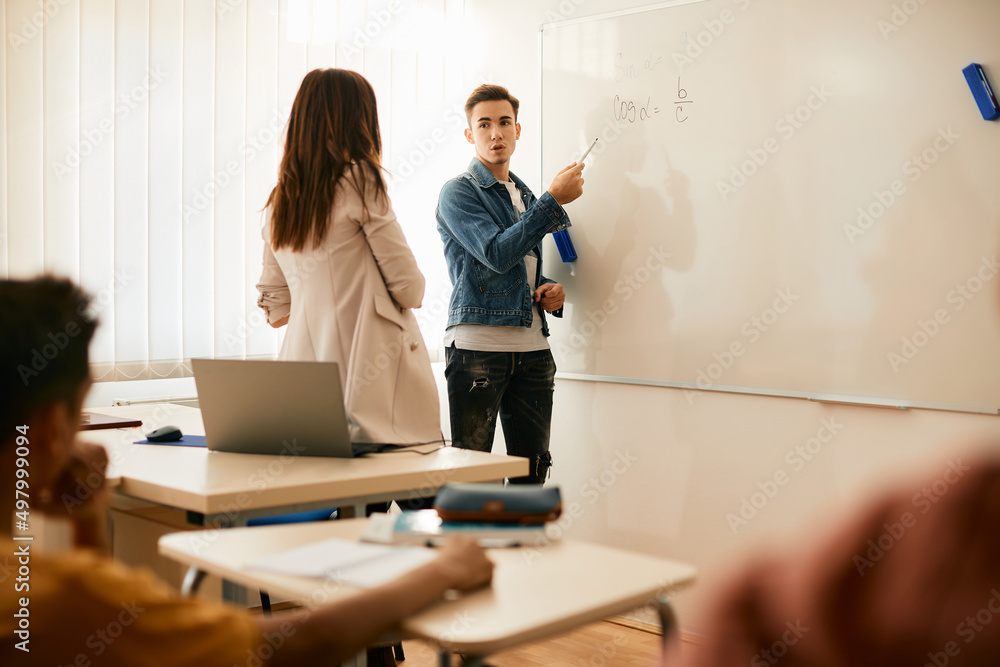 Teenage boy analyzing formula on whiteboard with math teacher during a ...