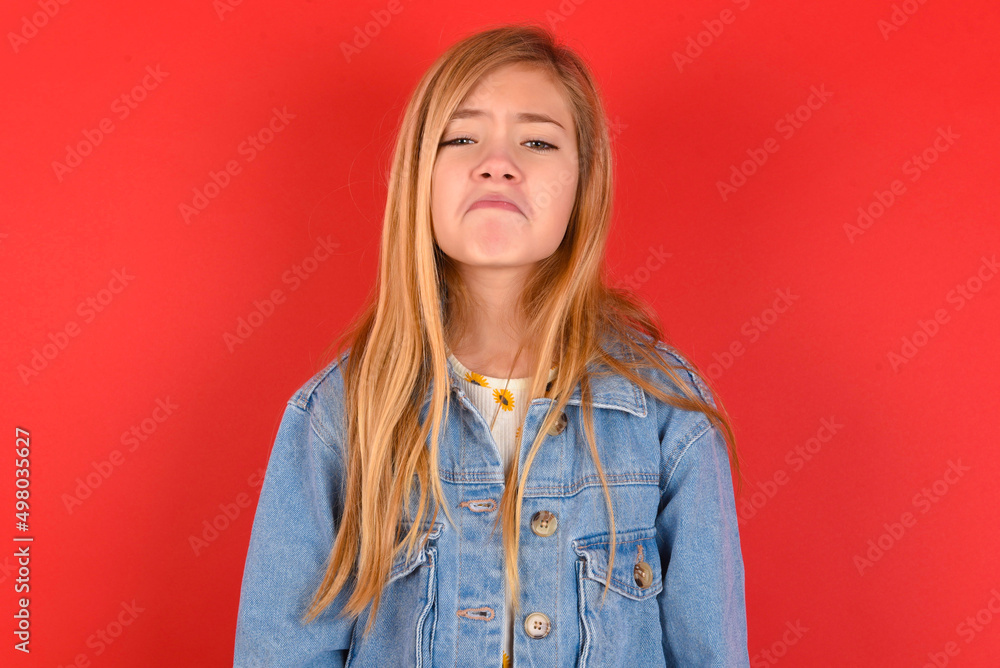 Displeased upset blonde little kid girl wearing denim jacket over red ...