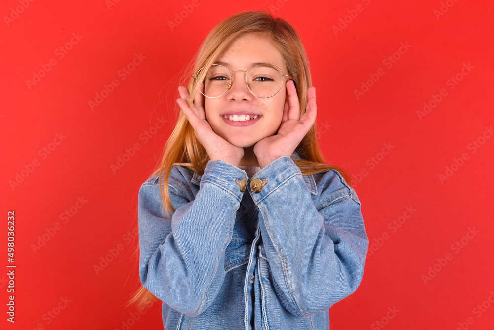 Happy blonde little kid girl wearing denim jacket over red background ...