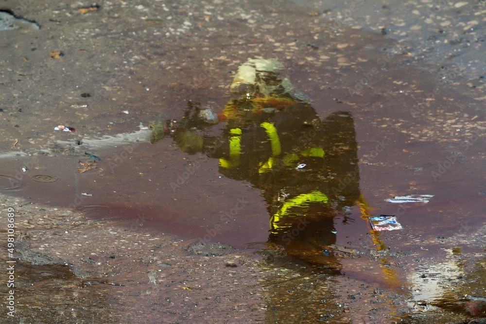 Reflection of a firefighter in a pool while extinguishing a waste fire ...
