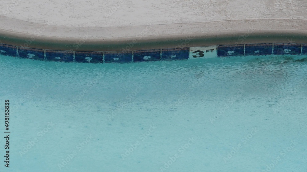 Rain drops falling on water surface of blue swimming pool, rainy day in ...