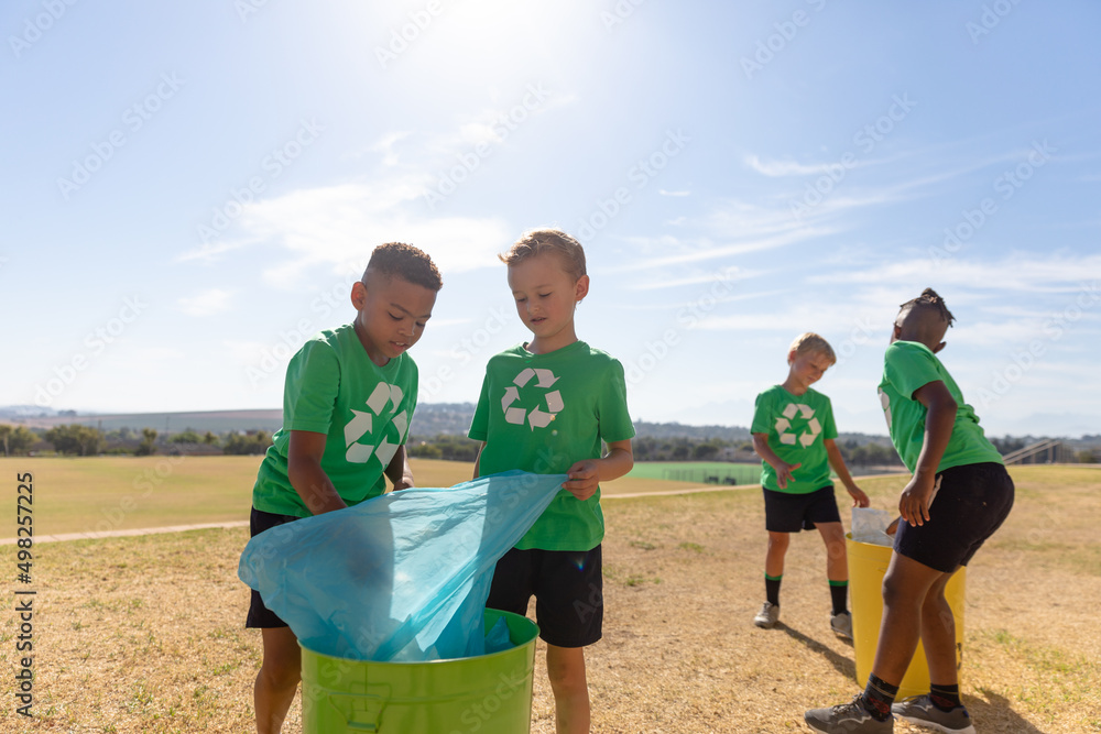 Multiracial elementary schoolboys putting garbage bags in garbage bin ...