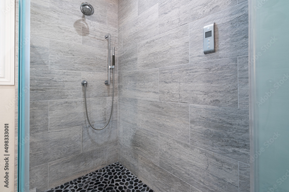 Walk-in shower with smooth gray tile walls and pebble rock flooring ...
