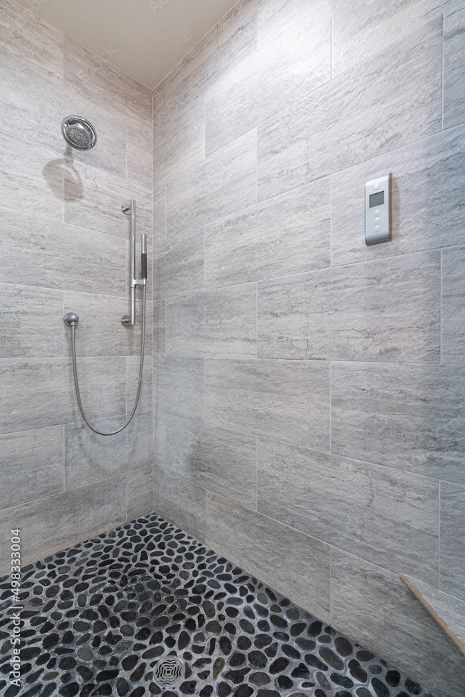 Walk-in shower with smooth gray tile walls and pebble rock flooring ...