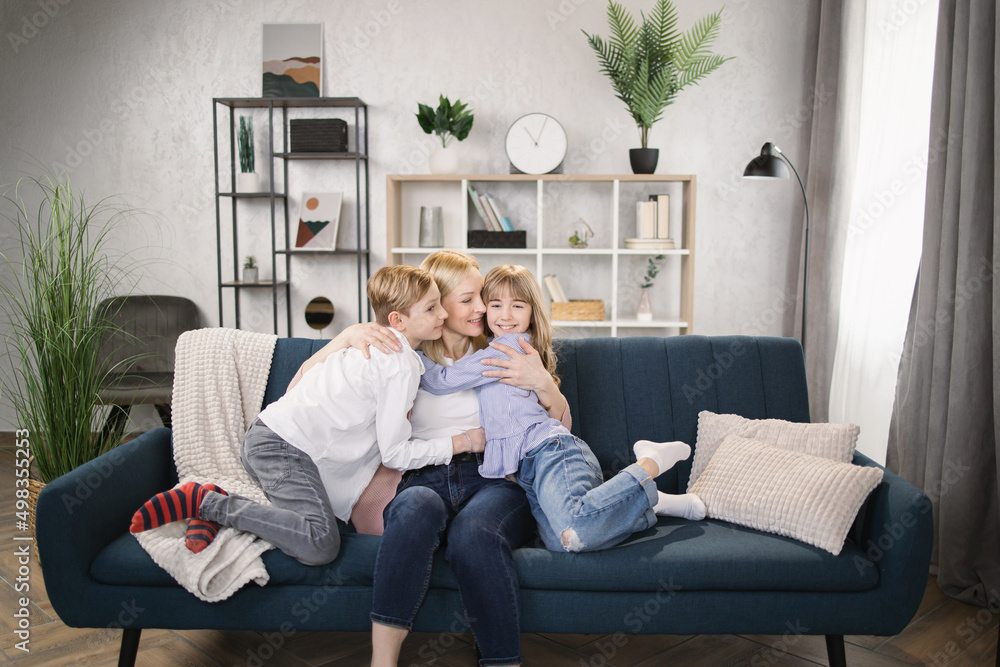 Happy little kids sit on couch hug cuddle excited young mom or nanny ...