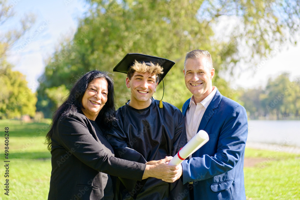 Young recently graduated boy, dressed in cap and gown, with his degree ...