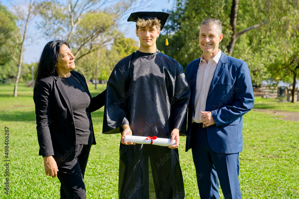 Young recently graduated boy, dressed in cap and gown, with his degree ...