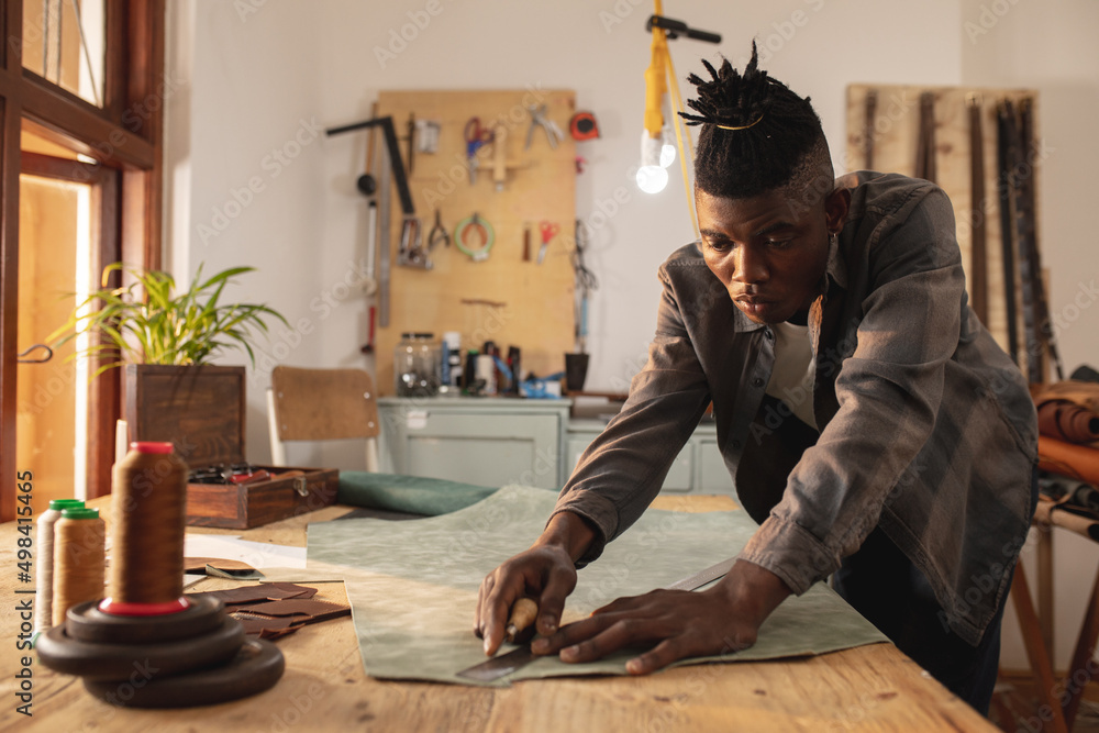 African american young craftsman cutting leather with equipment and ...